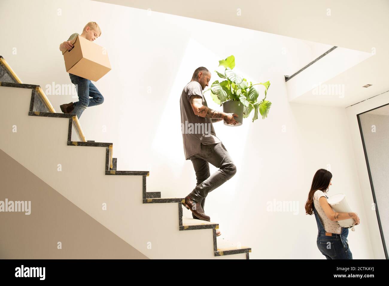 Family carrying various objects while moving down on steps in new home ...