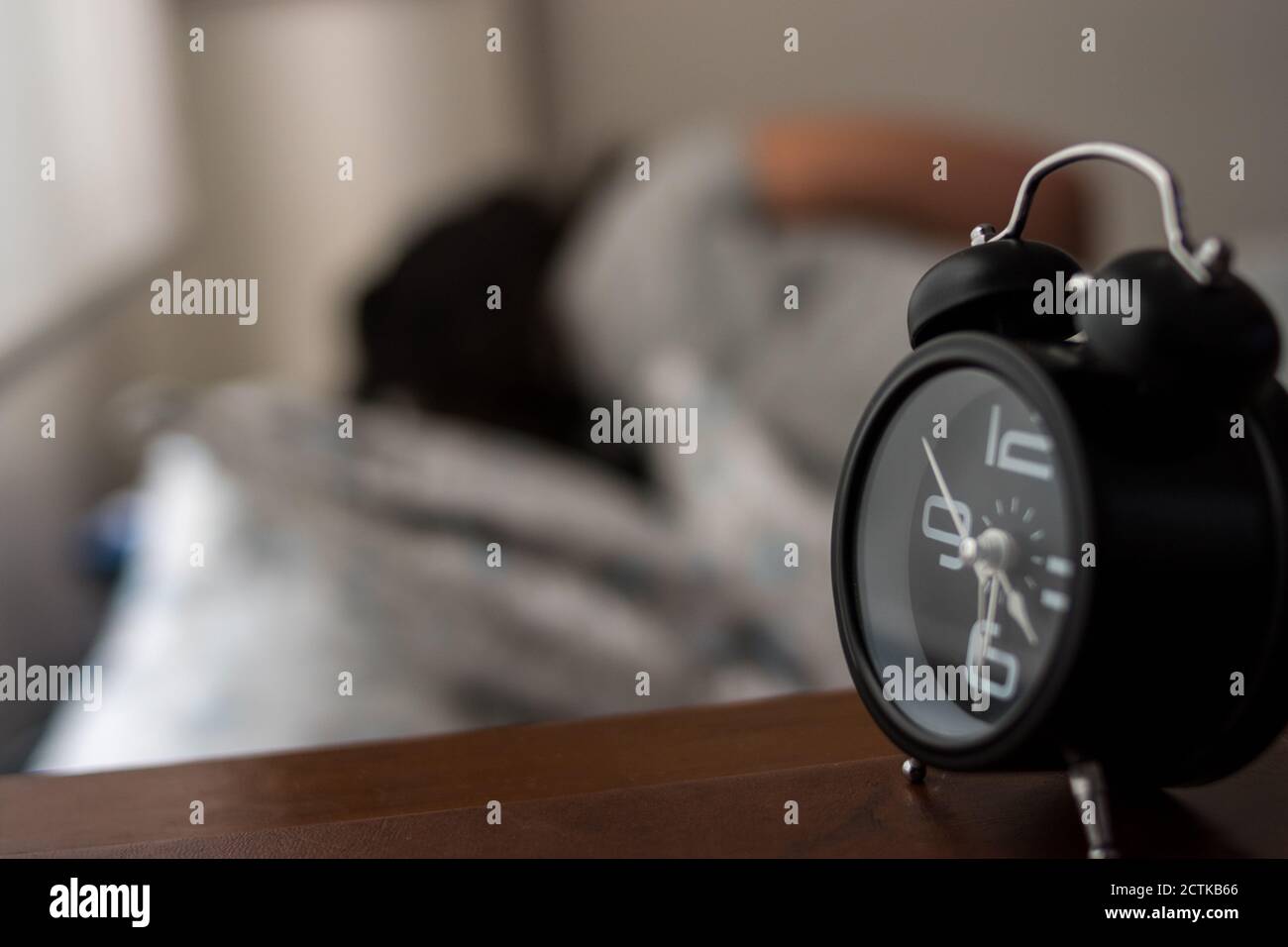 Little black clock in a white bedroom with a person sleeping at ...