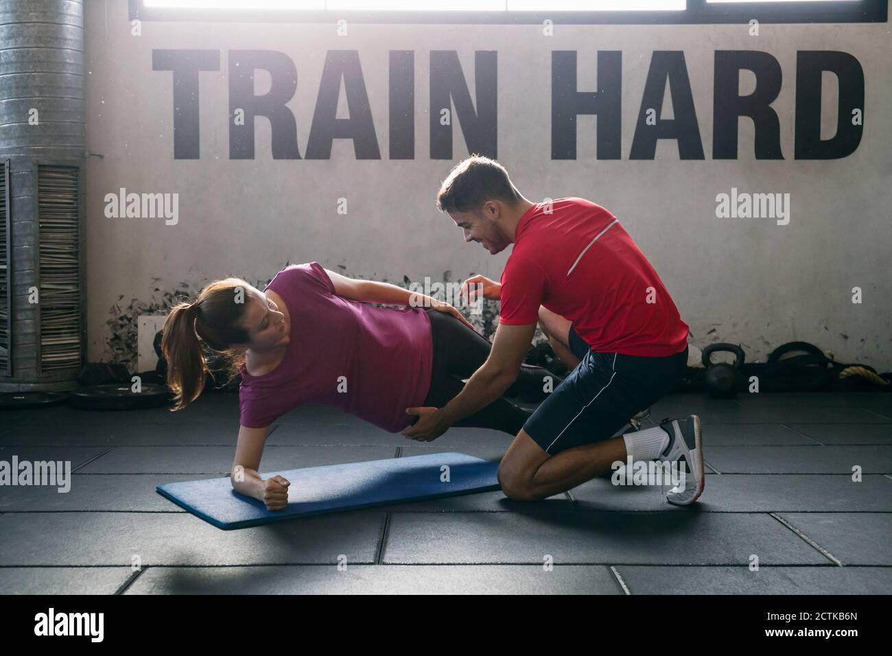 Fitness instructor assisting female athlete in practicing plank ...