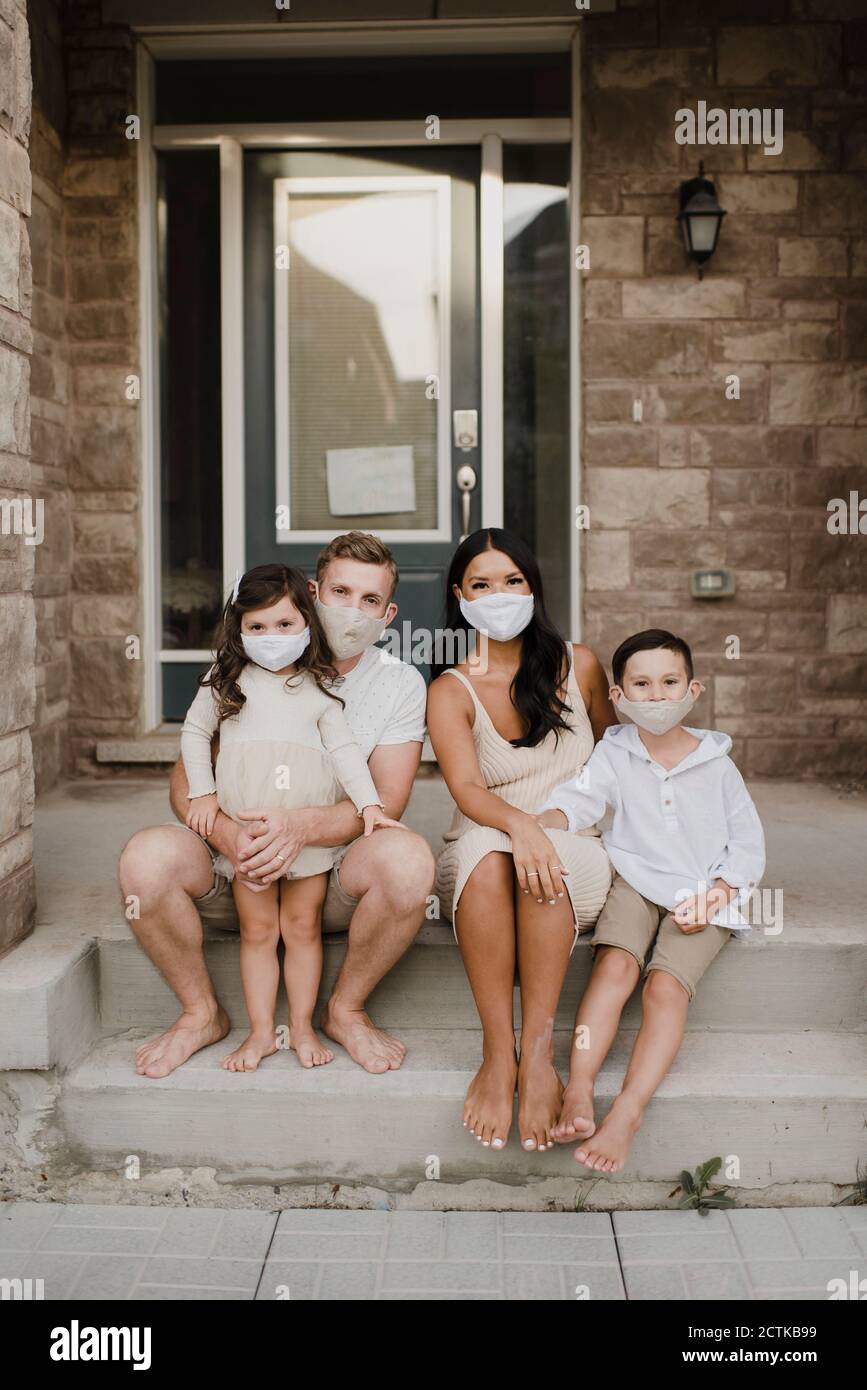 Family with kids wearing protective face mask while sitting on steps ...