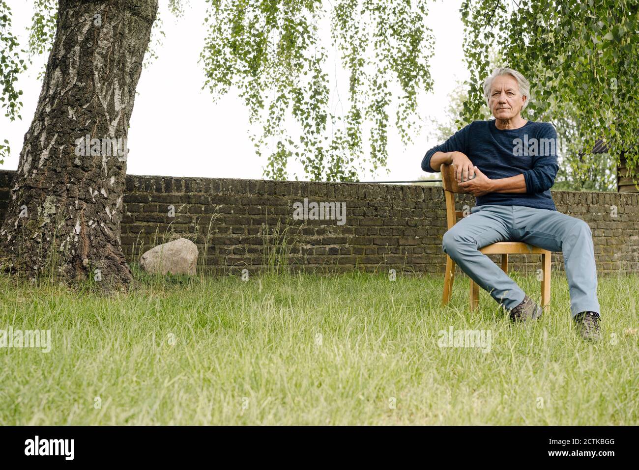 Contemplating man sitting on chair against brick wall in backyard Stock ...