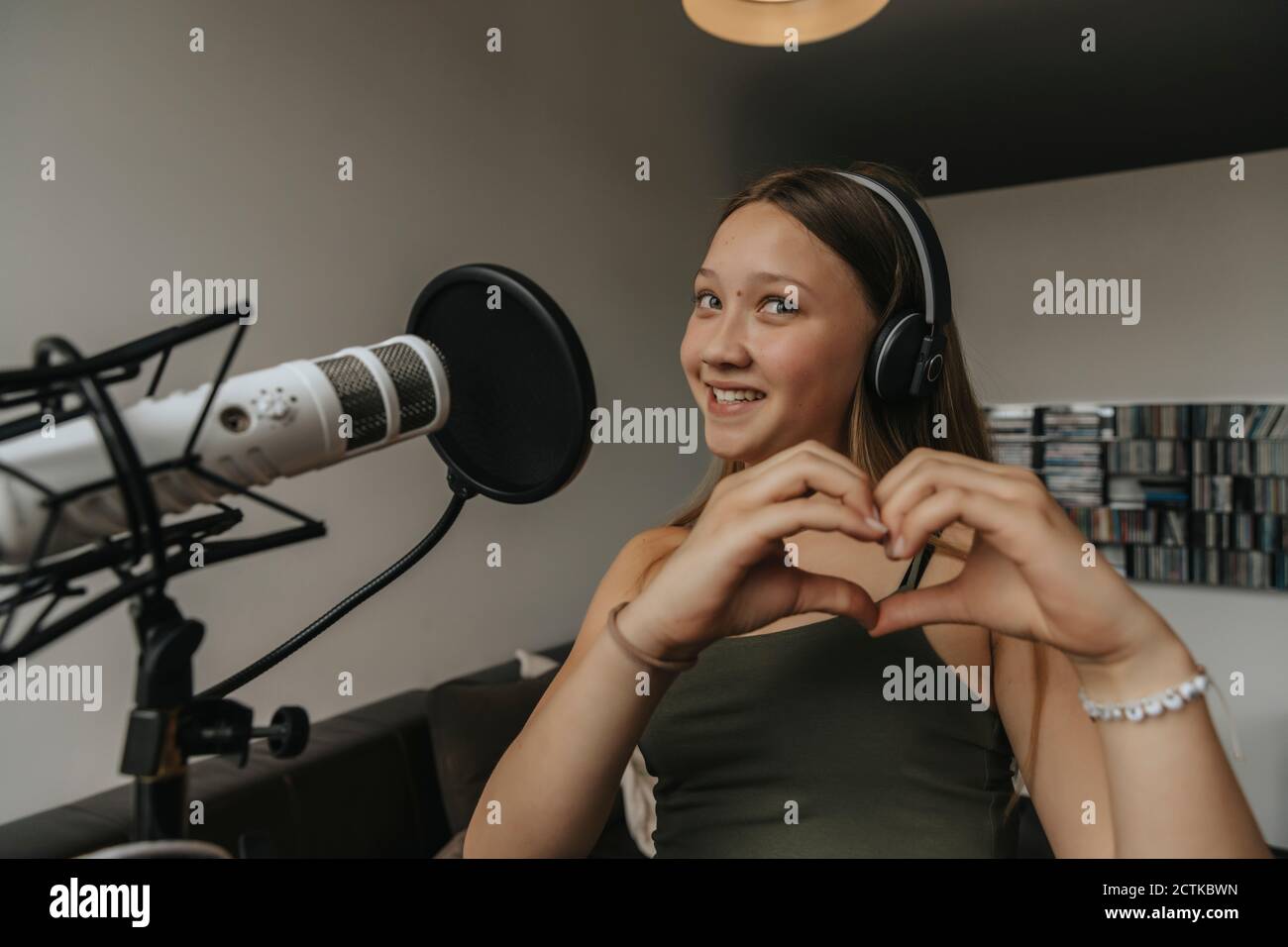 Smiling teenage girl making heart shape while singing in recording ...
