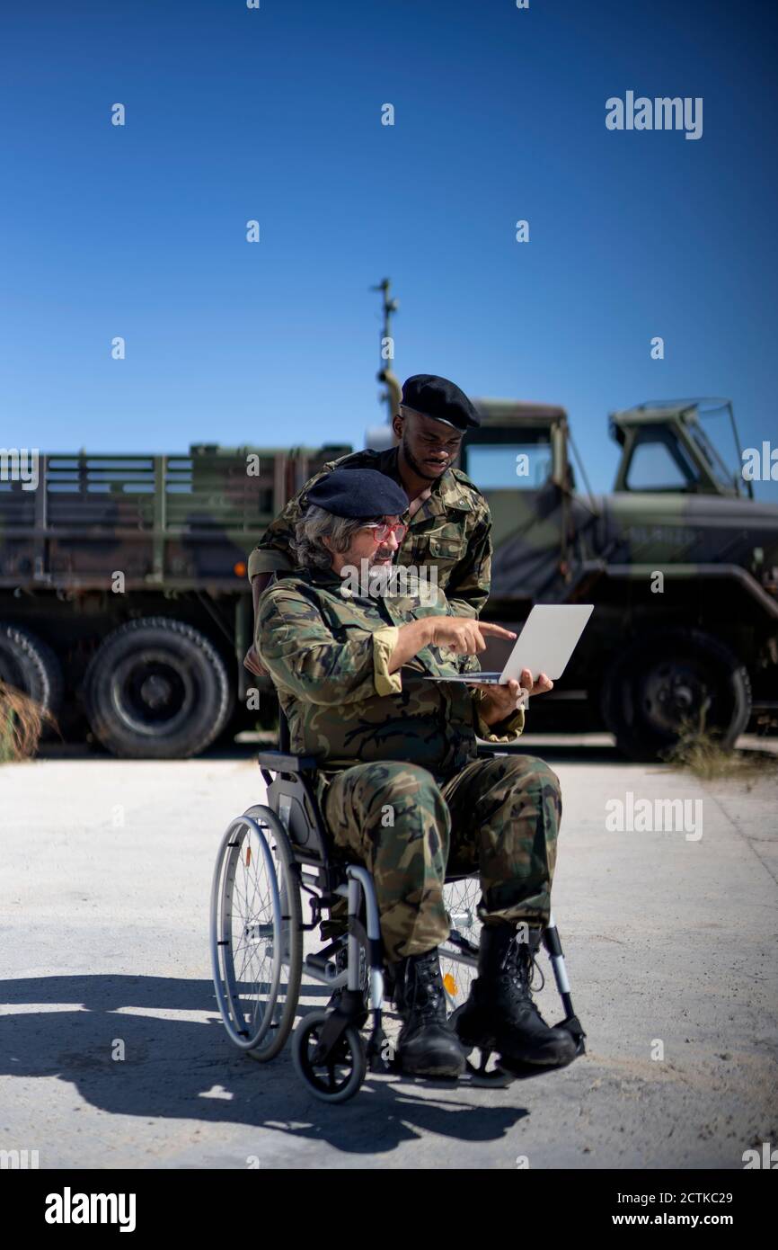 Disabled military officer working on laptop with colleague during sunny ...