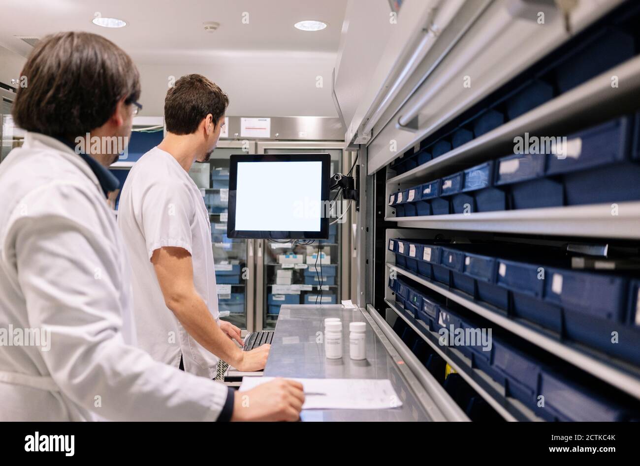 Male doctors using computer while standing in pharmacy at hospital ...