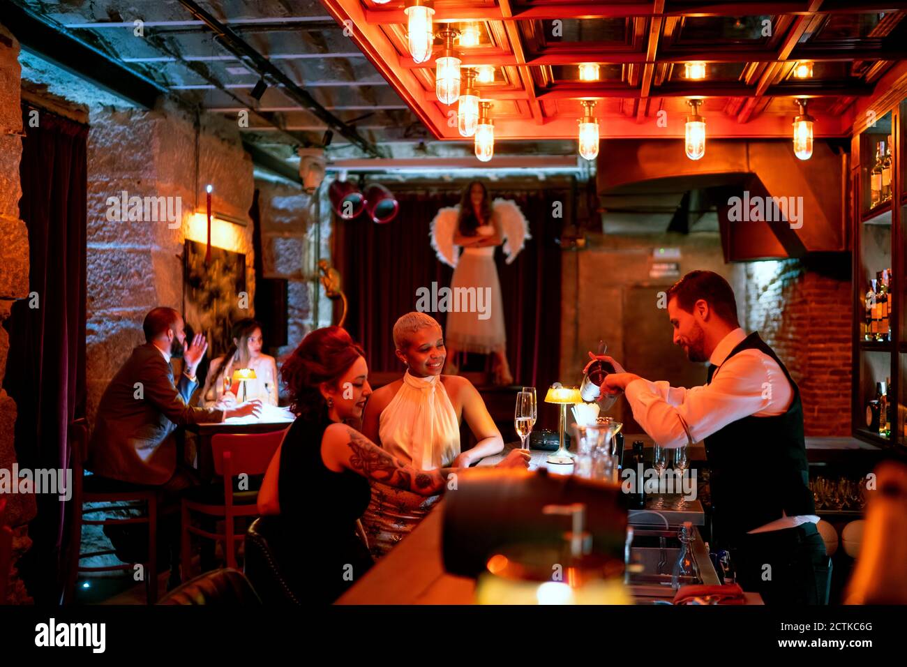 Women standing at bar counter with friends sitting in background at pub ...