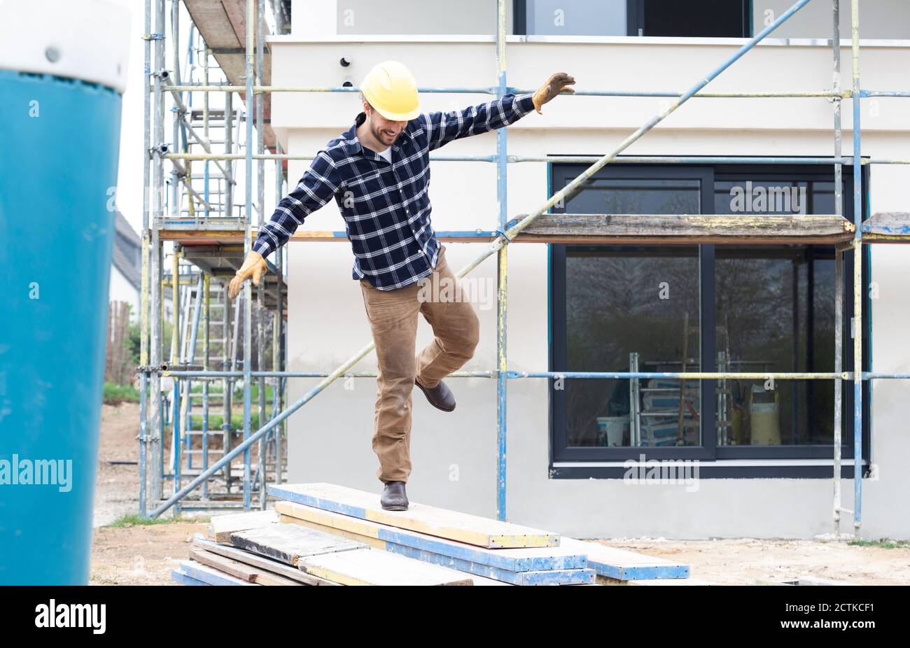 Construction worker with arms outstretched walking on wood against ...