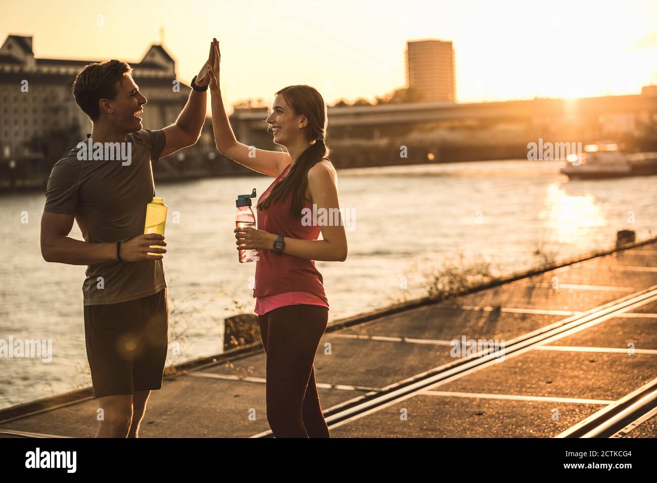 Smiling friends with water bottle giving high-five at harbor Stock ...