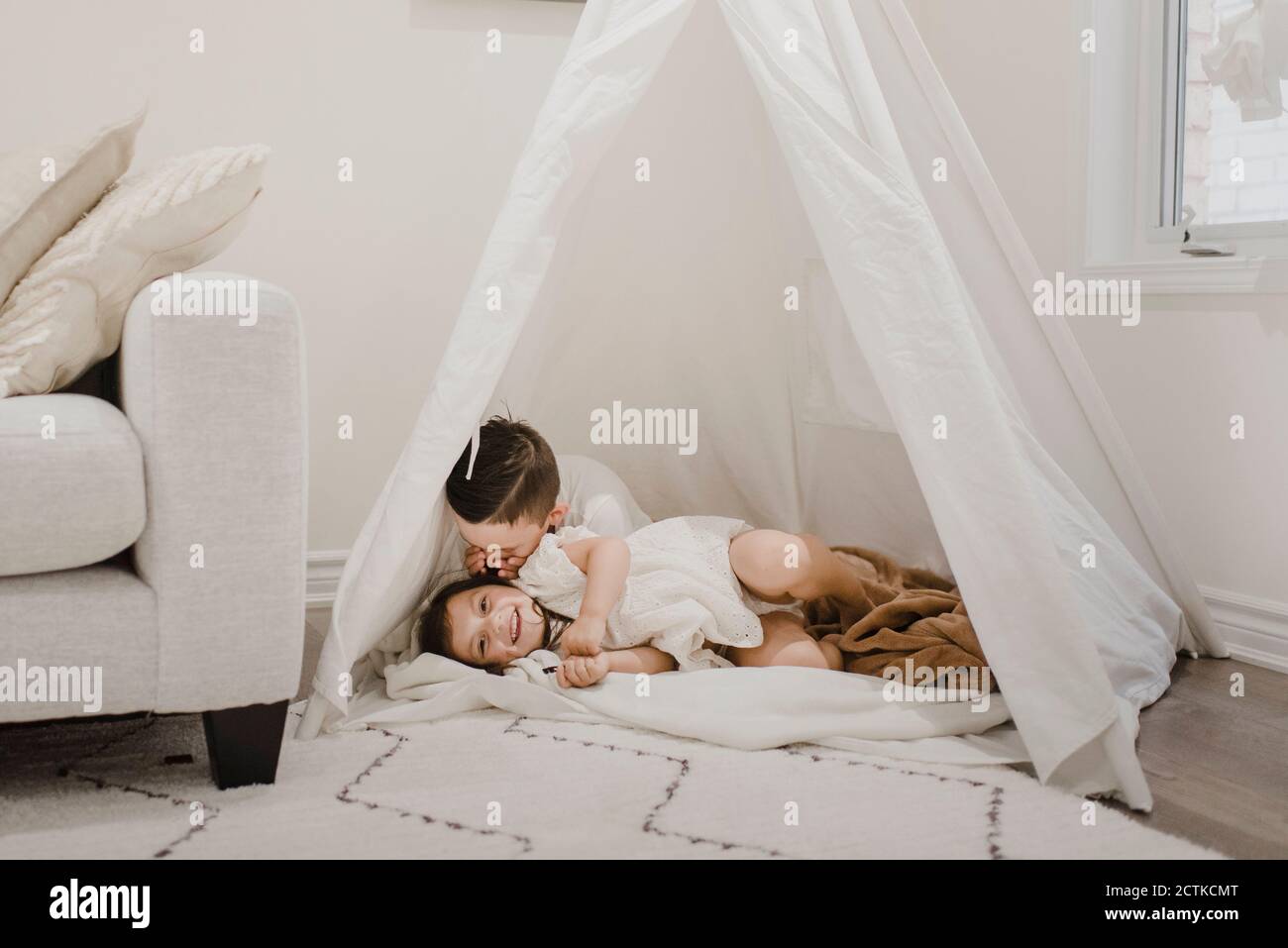 Brother whispering in sister's ear inside tent in living room Stock ...