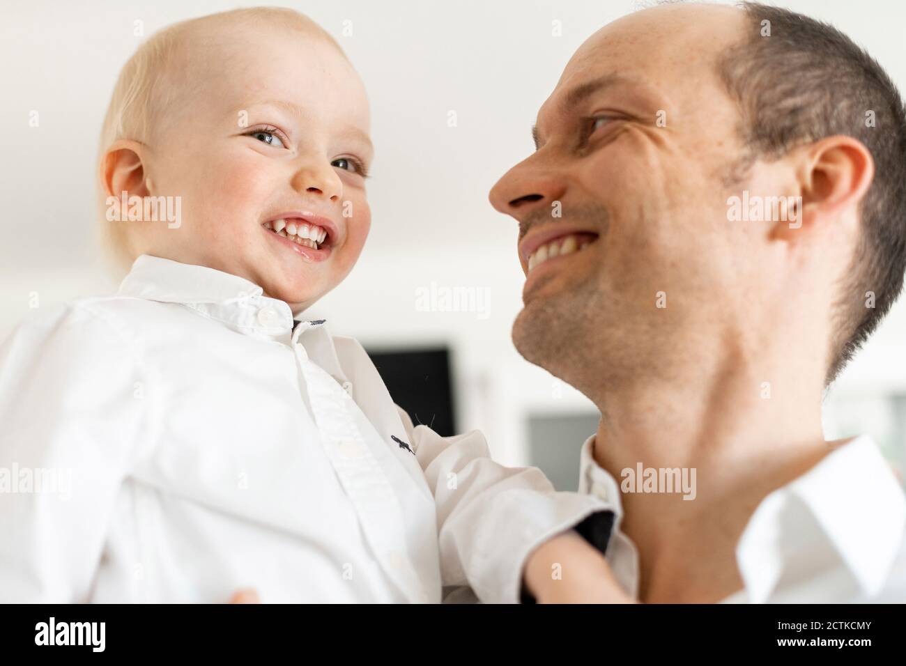 Father smiling while looking at baby boy while standing at home Stock ...