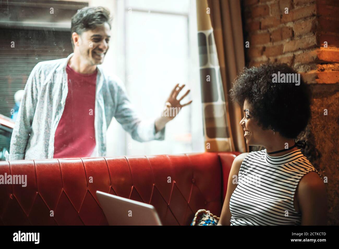 Woman looking at boyfriend through window while sitting with laptop in ...