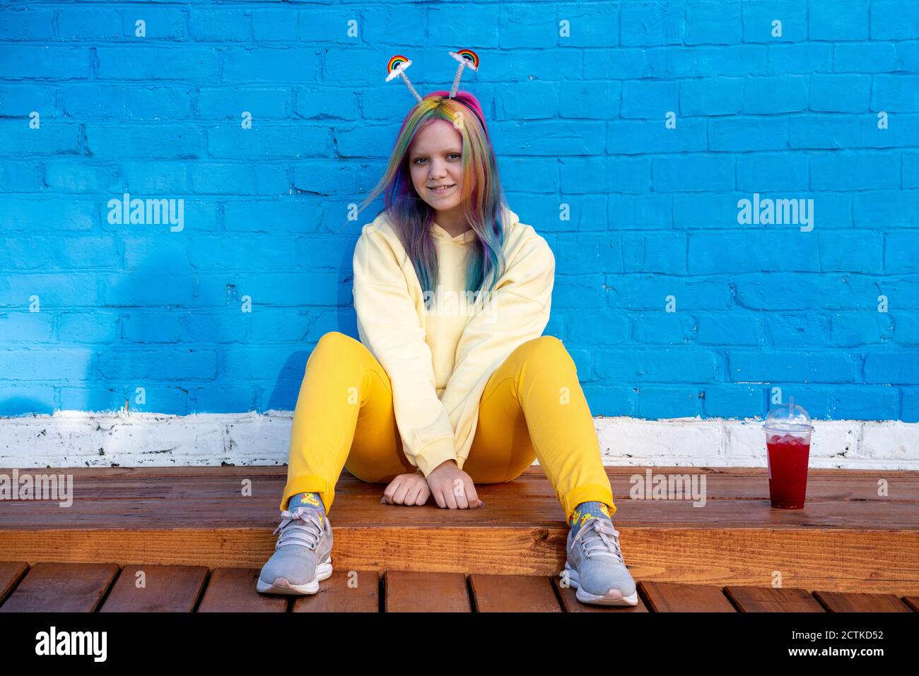 Young woman with dyed hair and rainbow alice band in front of blue wall ...