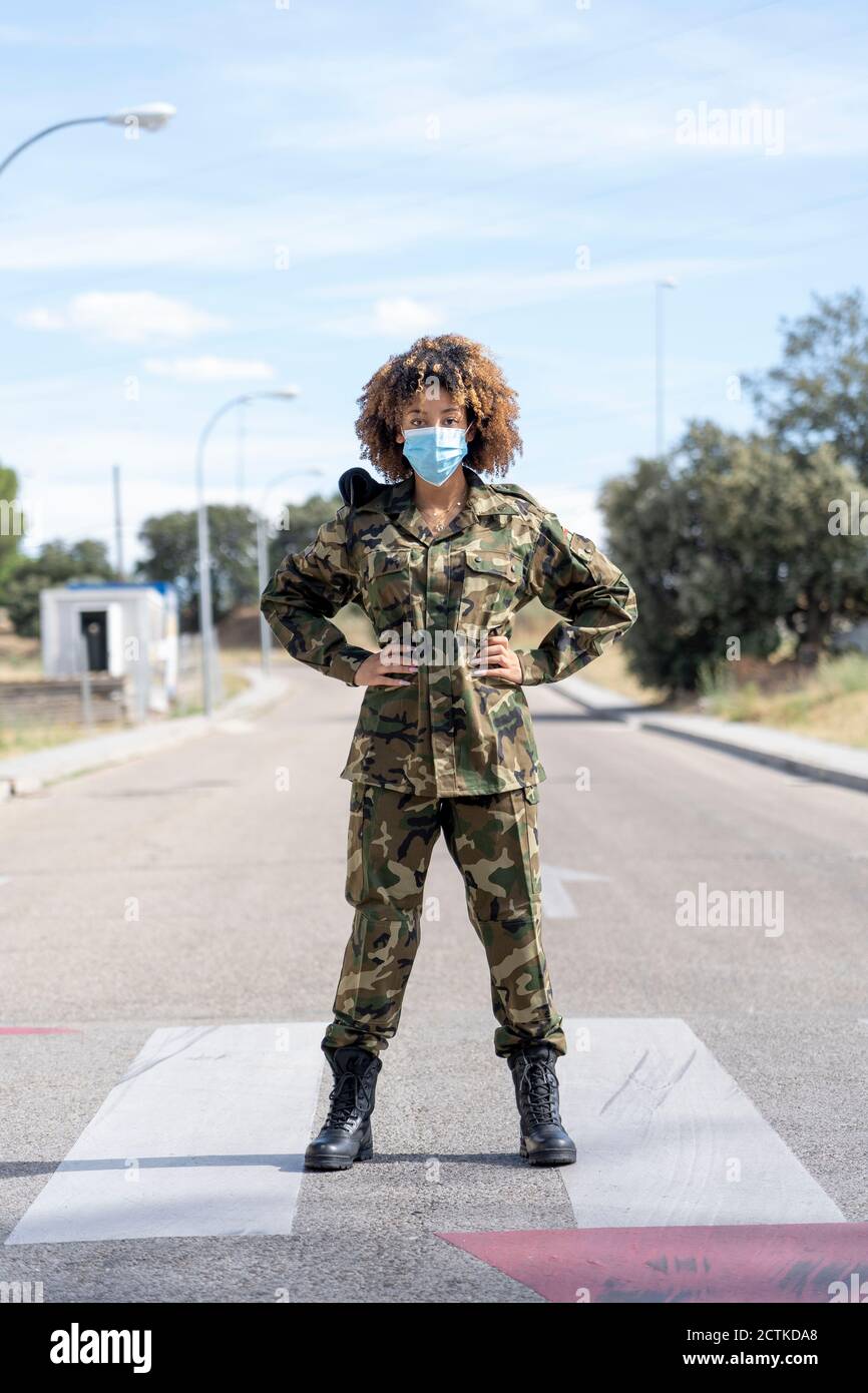 Female army soldier wearing protective face mask with hands on hip ...