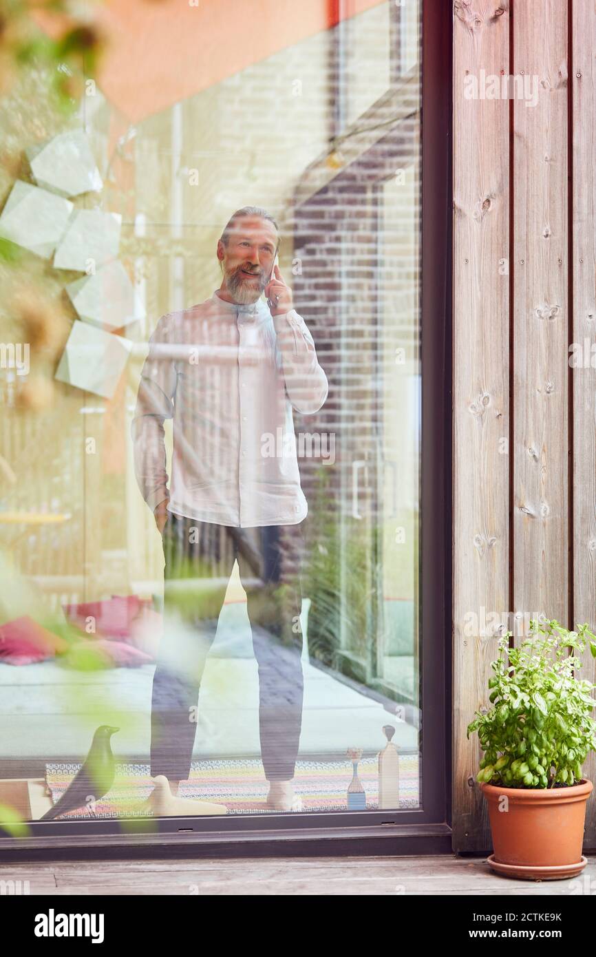 Man talking over mobile phone while standing in tiny house seen through ...