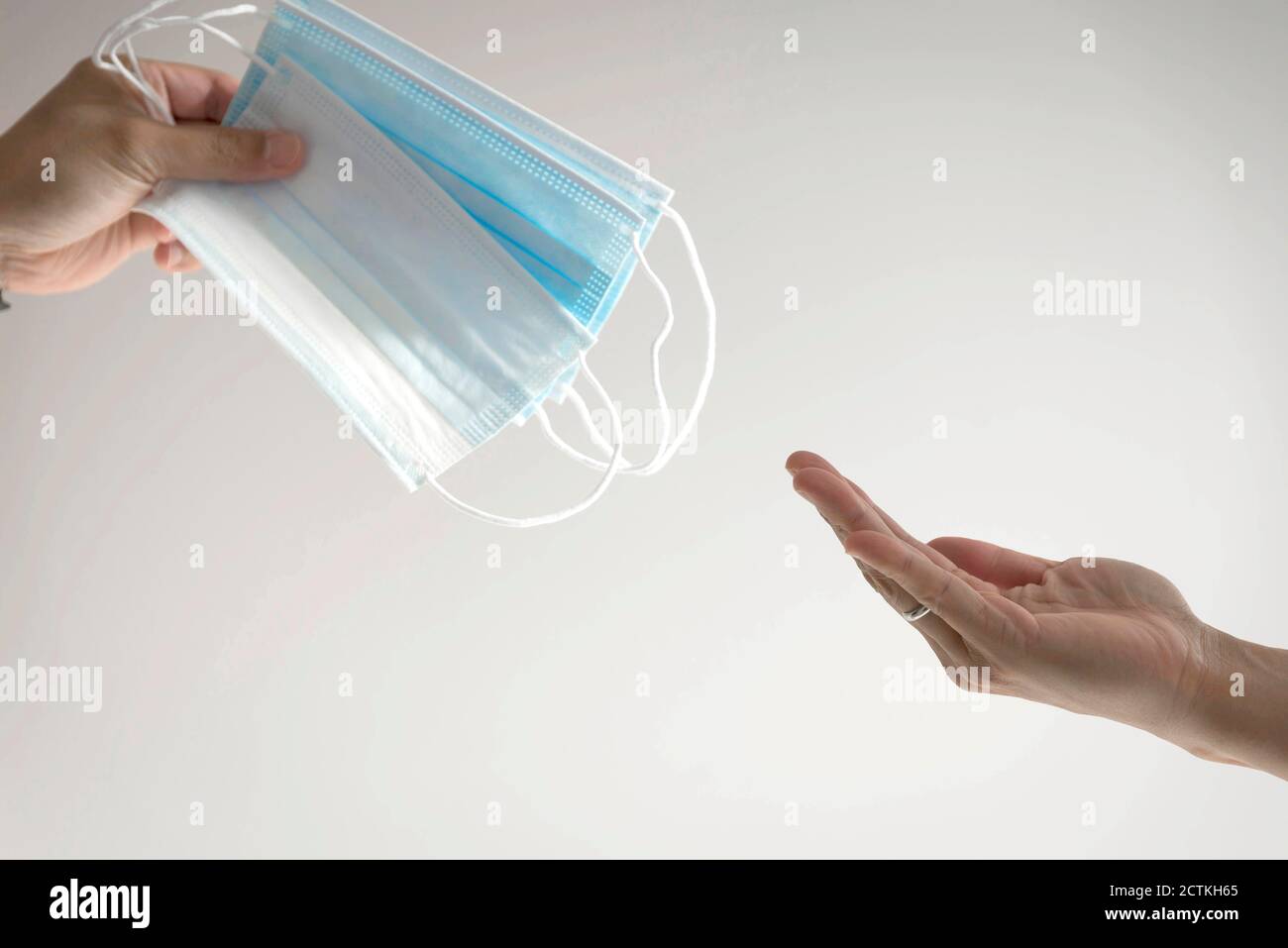 Mask being given to another hand on white background Stock Photo - Alamy