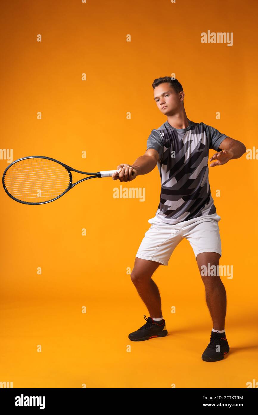 Full-length portrait of a tennis player man in action against orange ...