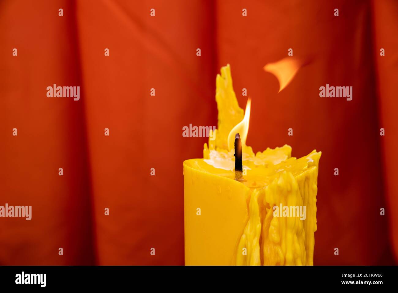 Close up to the melt yellow candle and fire flame with the red curtain ...