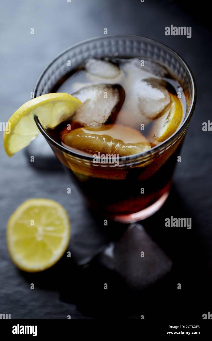Glass of cola with lemon and ice cubes. Dark stone background. Close up ...