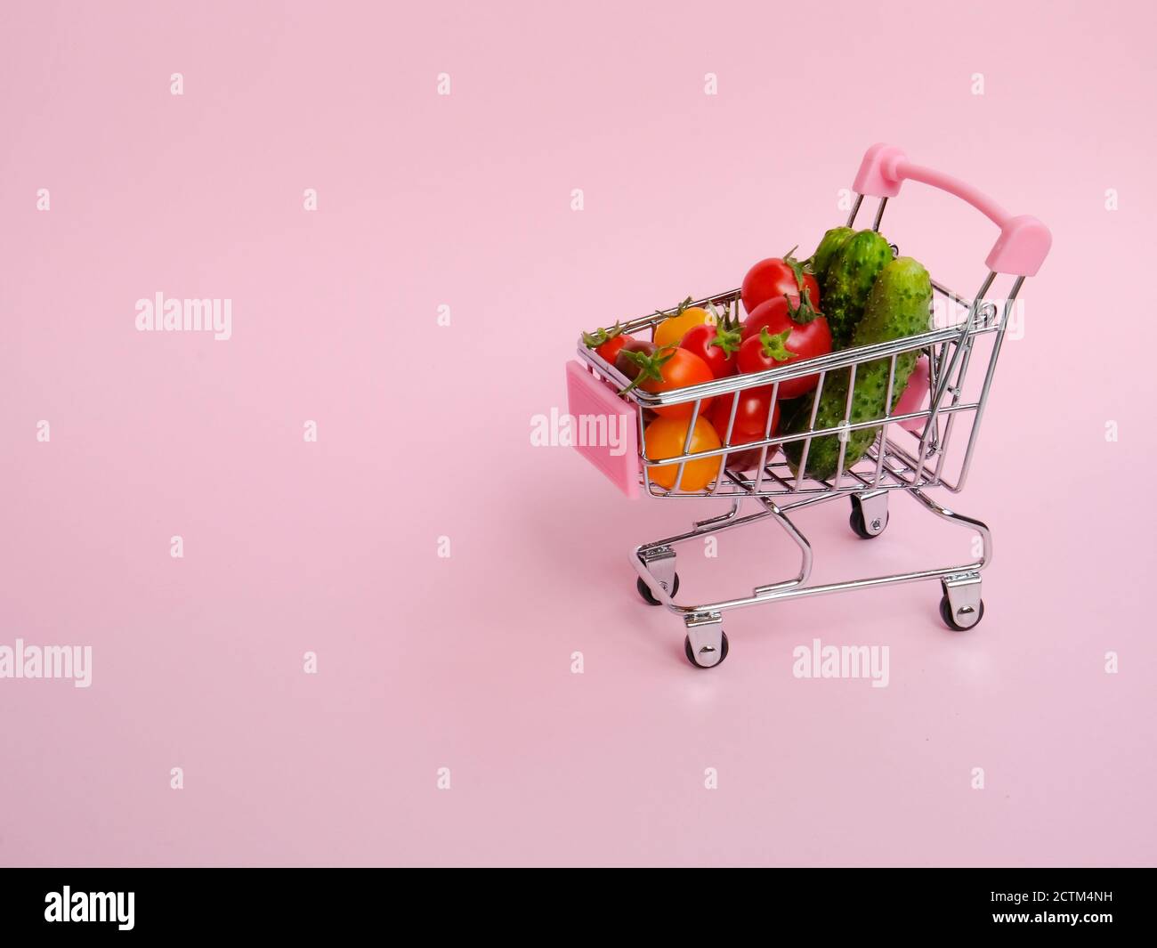 Pink grocery cart full of tomatoes and cucumbers on pink background ...