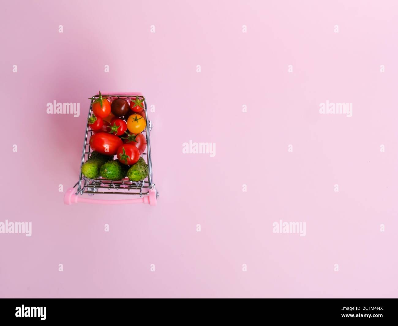 Pink grocery cart full of tomatoes and cucumbers on pink background ...