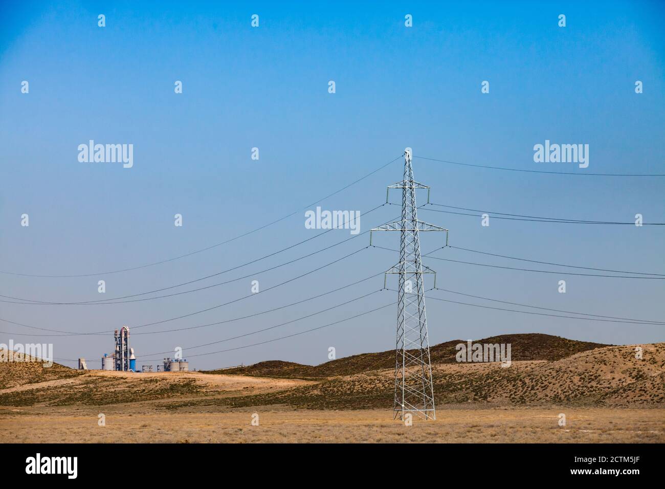 Grey cement plant tower and silo and electric pylon of power line on ...
