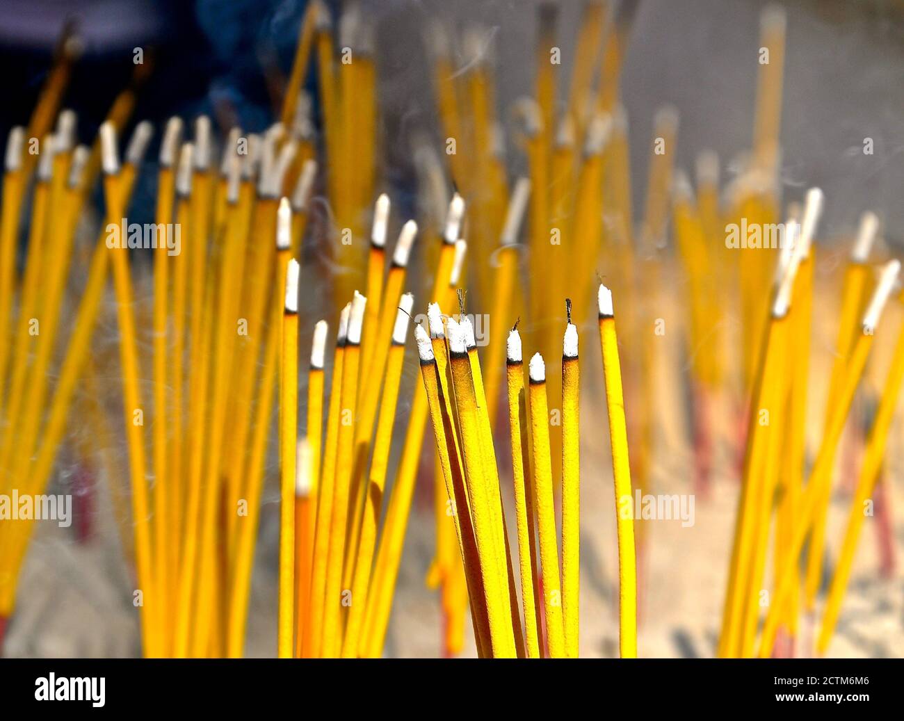 Close up perspective view of smouldering yellow incense sticks in a ...