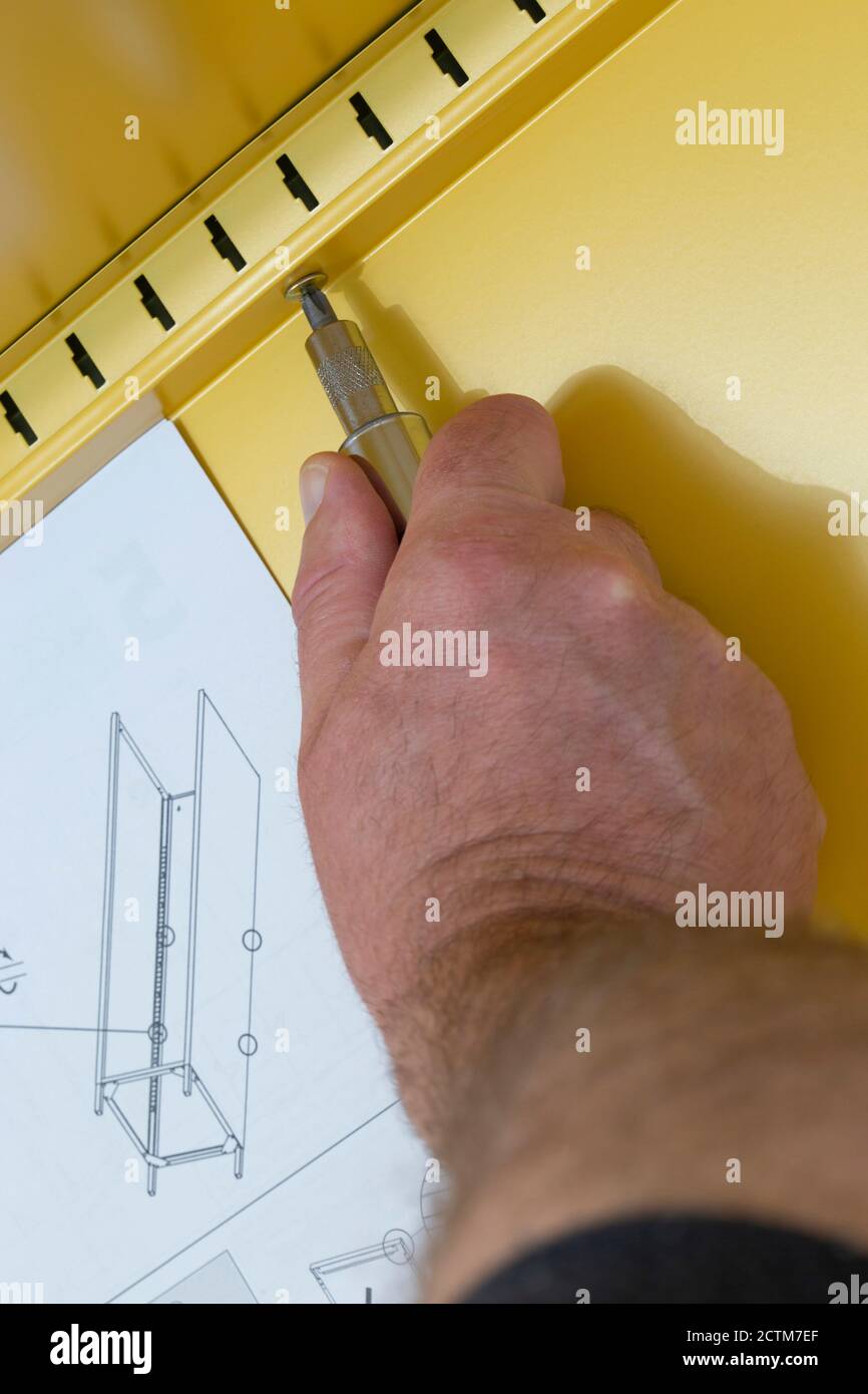 Man Assembling A Yellow Metal Cabinet With A Screwdriver And