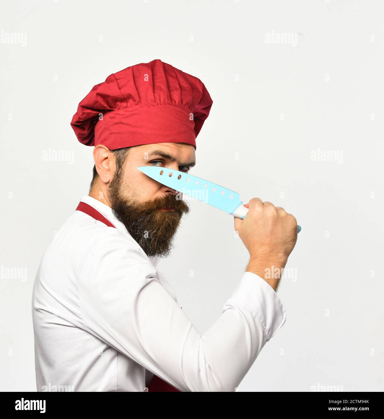 Chef looks through sharp blue knife. Cook with curious face in burgundy ...
