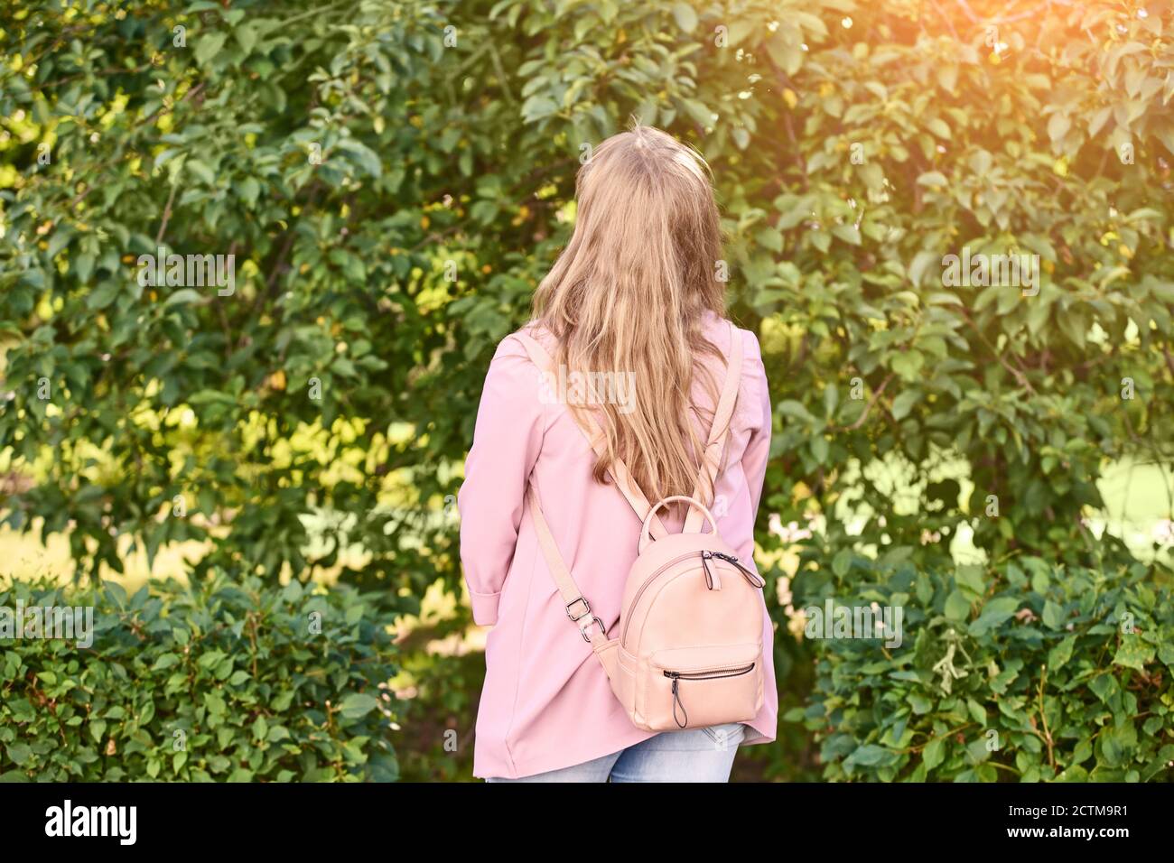 American portrait of schoolgirl. Summer park. Back view with backpack ...