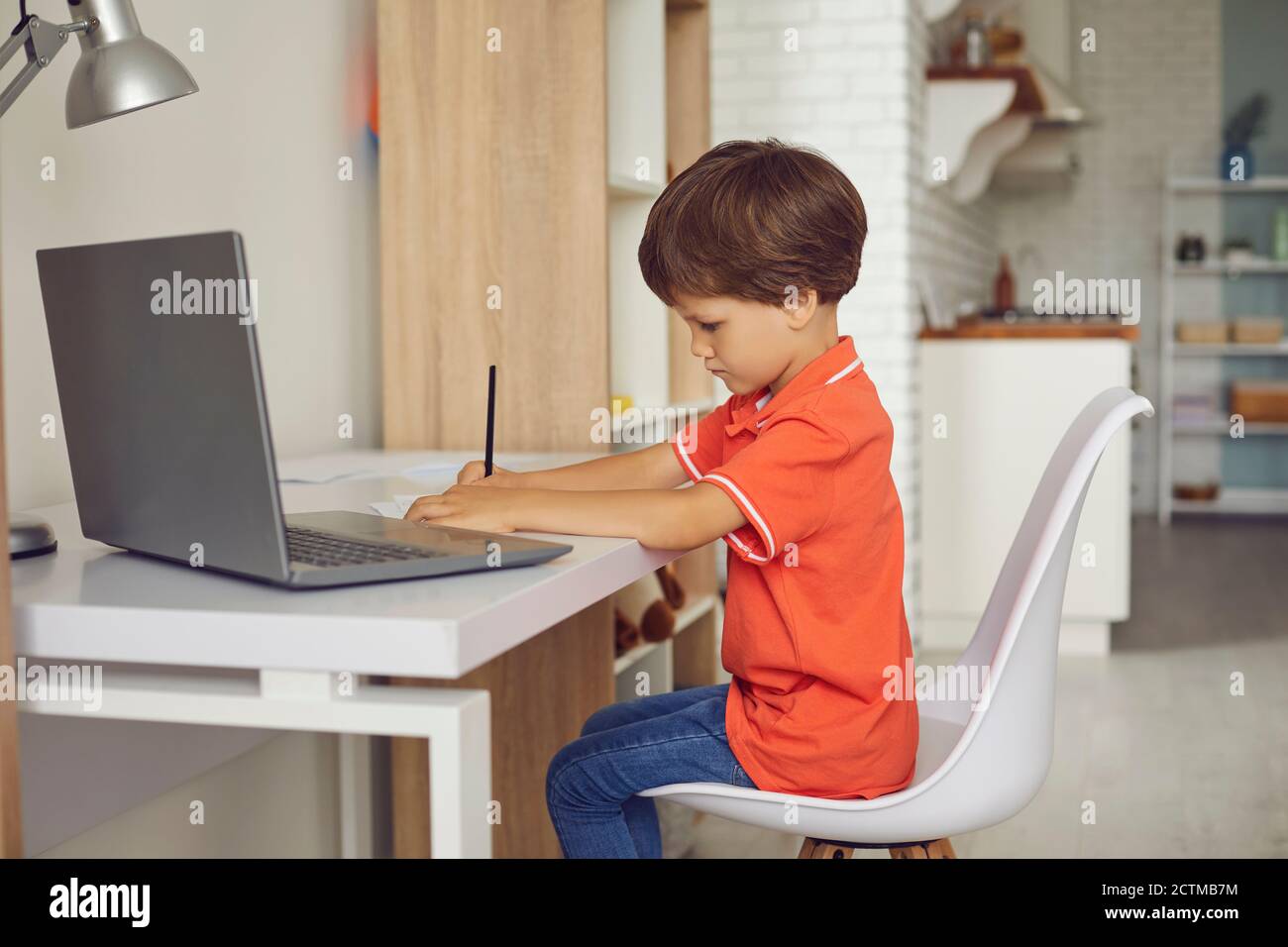 Concentrated boy doing homework using modern laptop computer sitting at ...