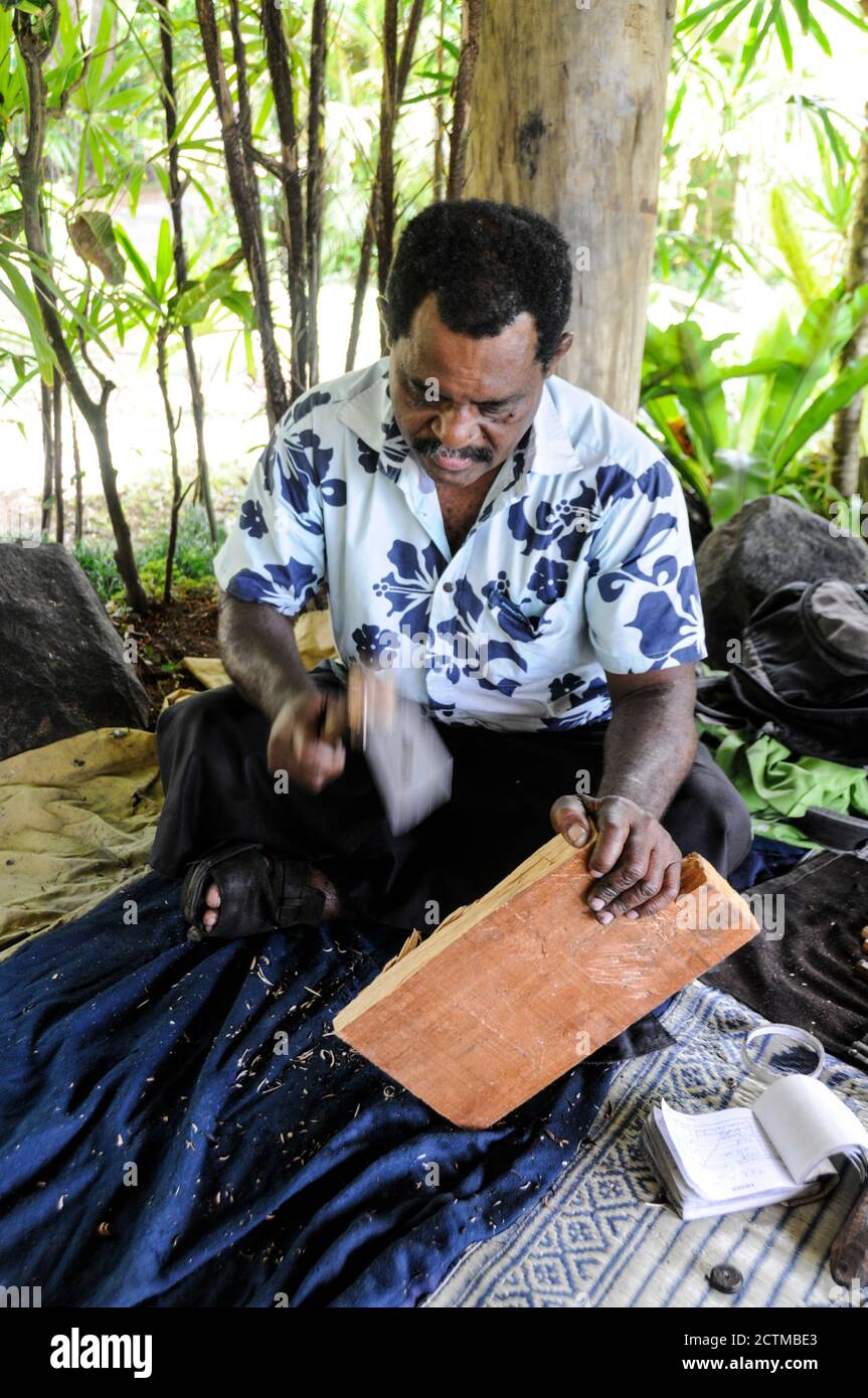 A Fijian woodcarver working on a piece of mahogany for tourists to buy ...