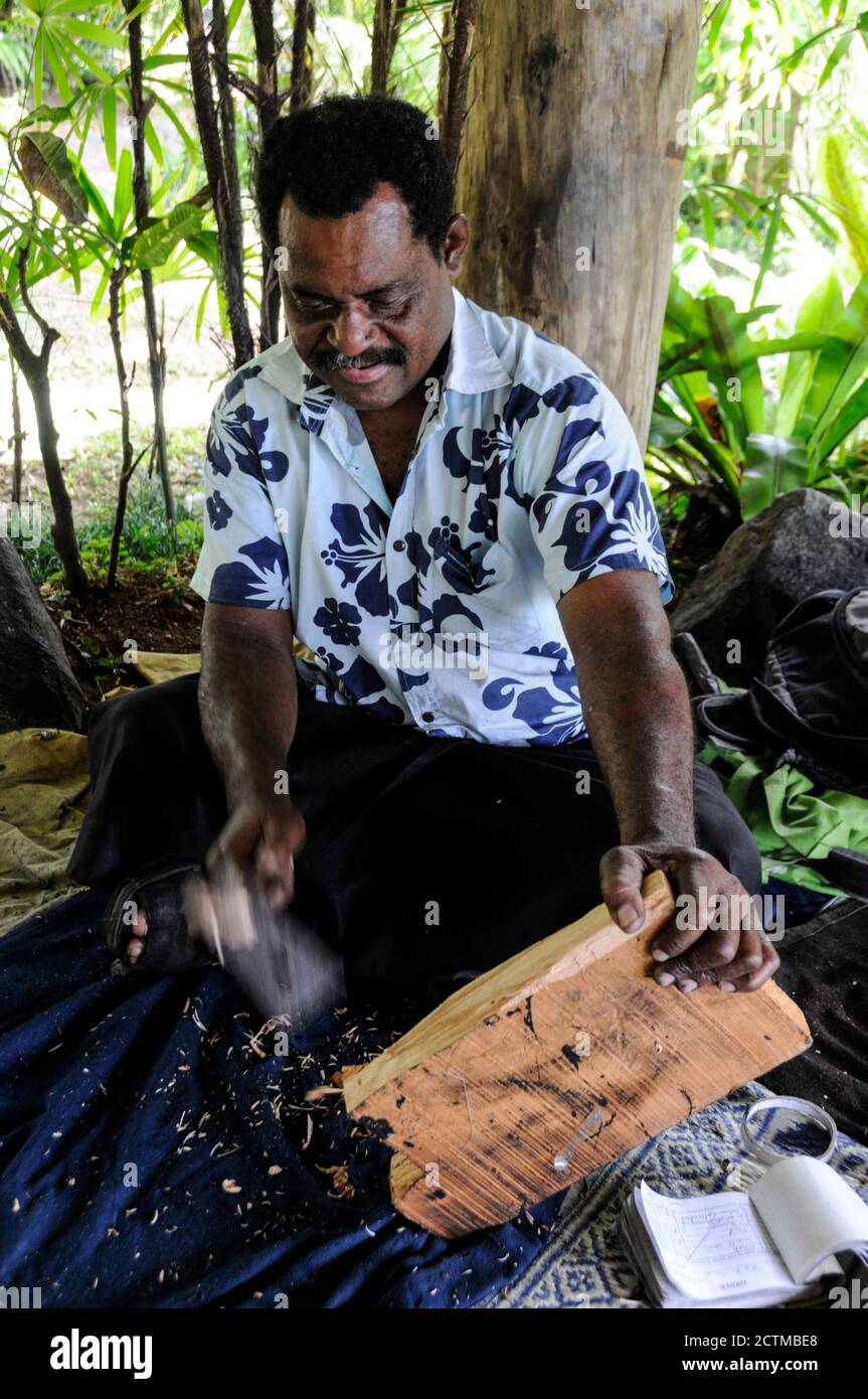 A Fijian woodcarver working on a piece of mahogany for tourists to buy ...