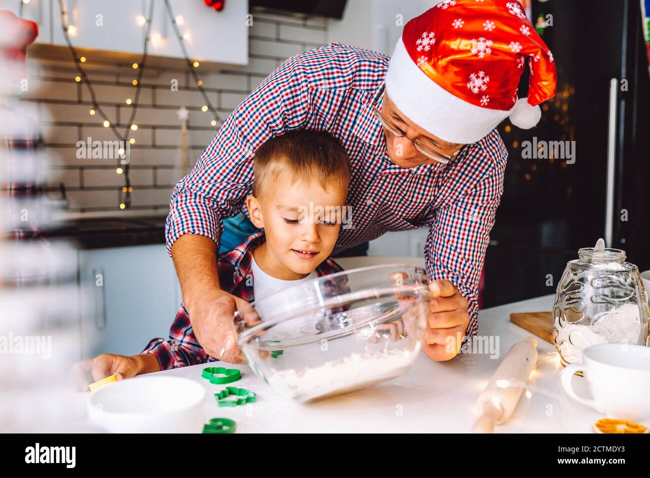 Happy family of father and son in Santa hats bake cookies in kitchen ...