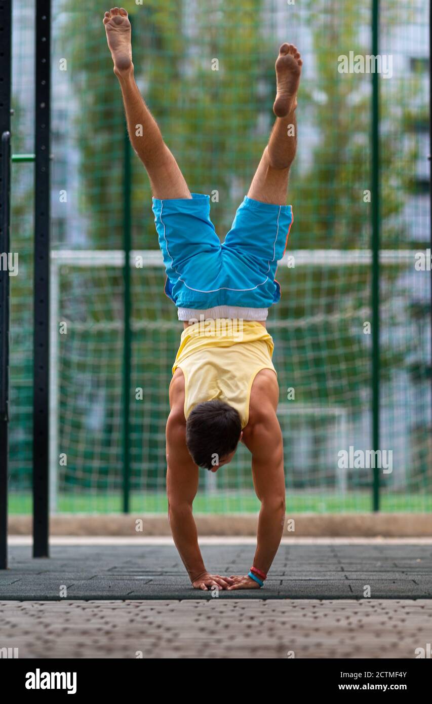 Young muscular barefoot male athlete doing a handstand outdoors at a ...