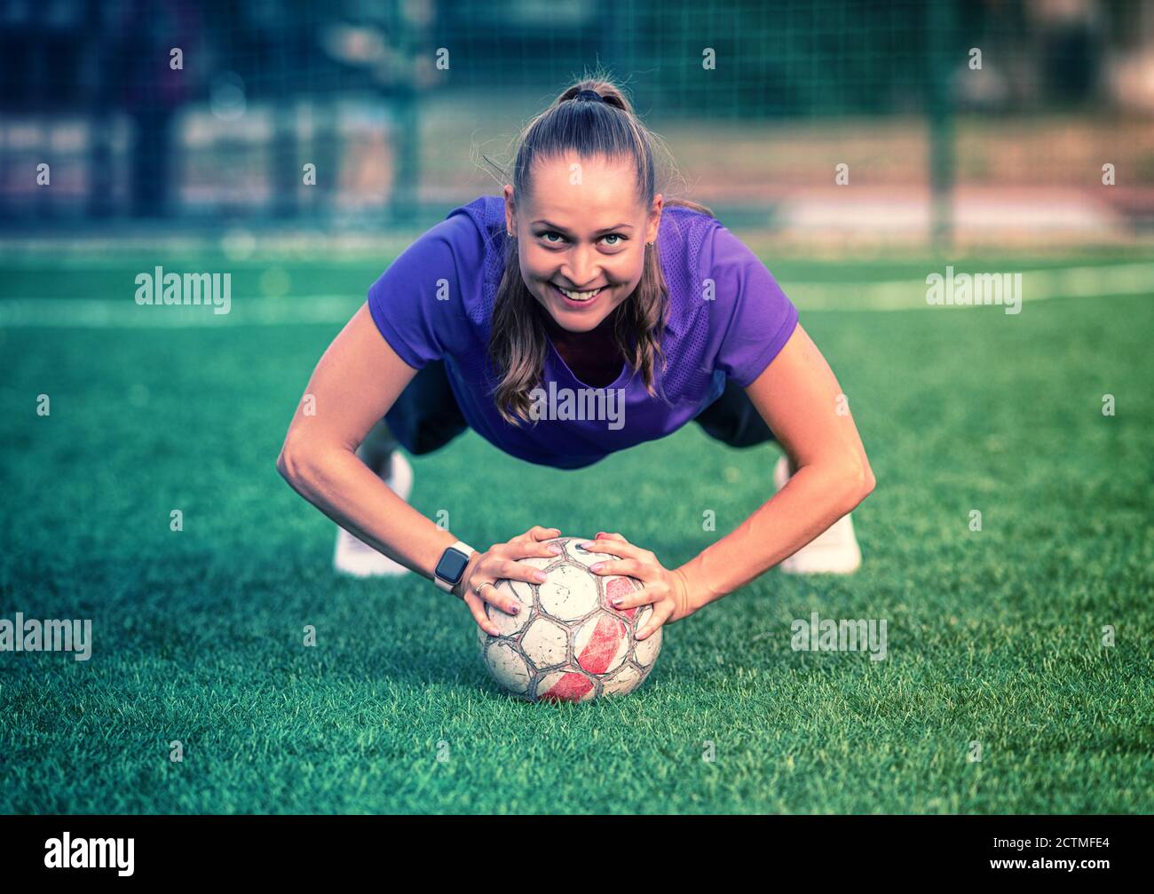 Happy smiling young female athlete with soccer ball in the yoga plank ...