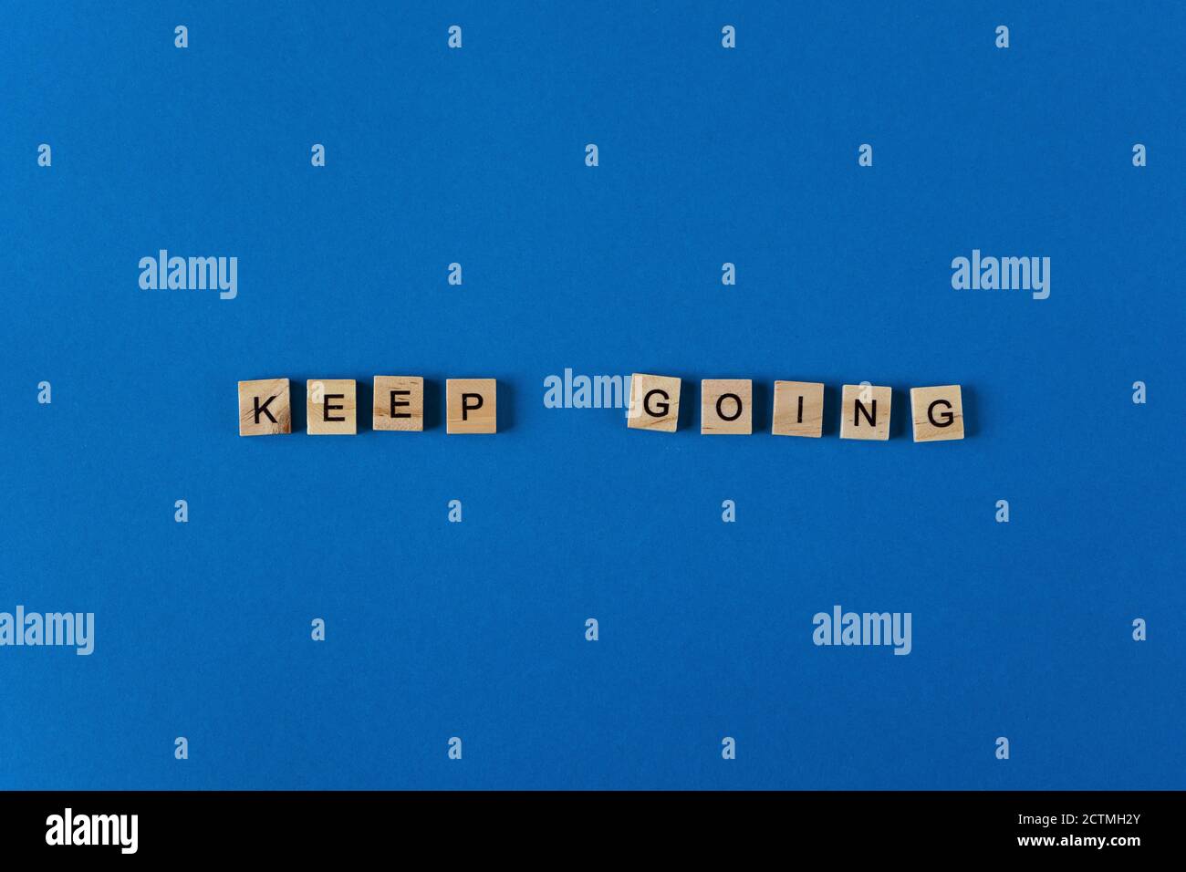 The phrase keep going is lined with wooden letters on ablue background ...