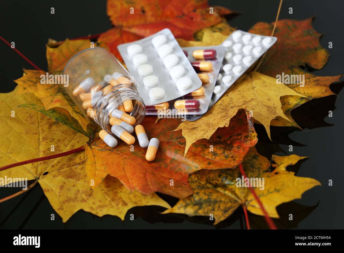 Pills on yellow and red maple leaves, bottle of capsules and blister ...
