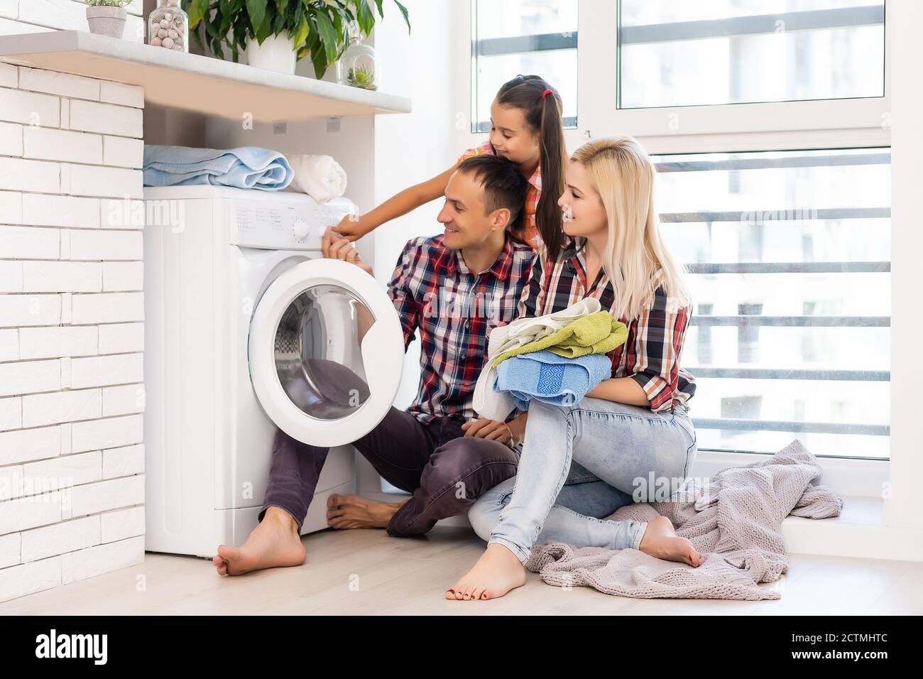 family mother, father and child girl little helper in laundry room near ...