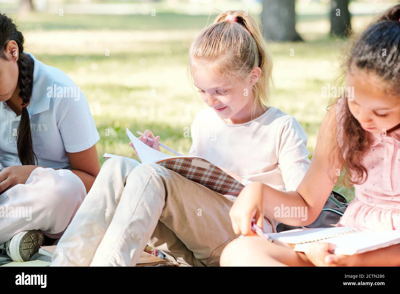 Curious blond girl sitting among classmates and checking notes in ...