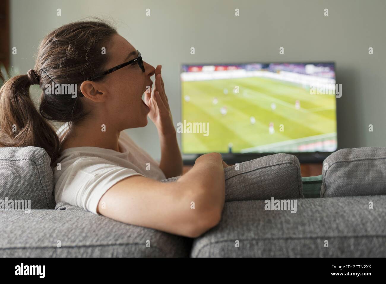 Woman watching football on TV, she is bored and yawning Stock Photo - Alamy