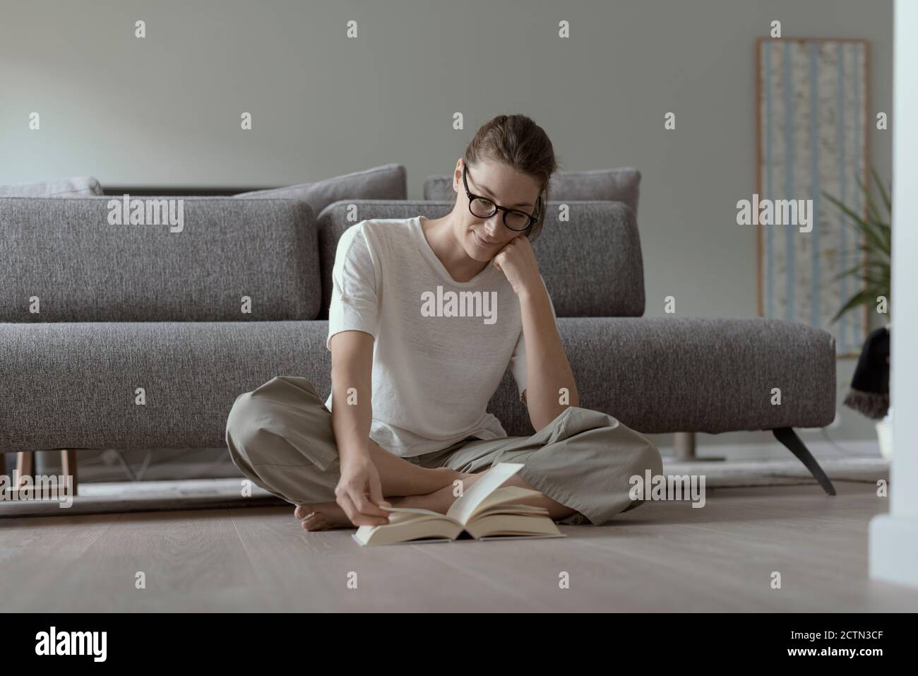 Happy serene woman sitting on the floor and reading a book, she is ...