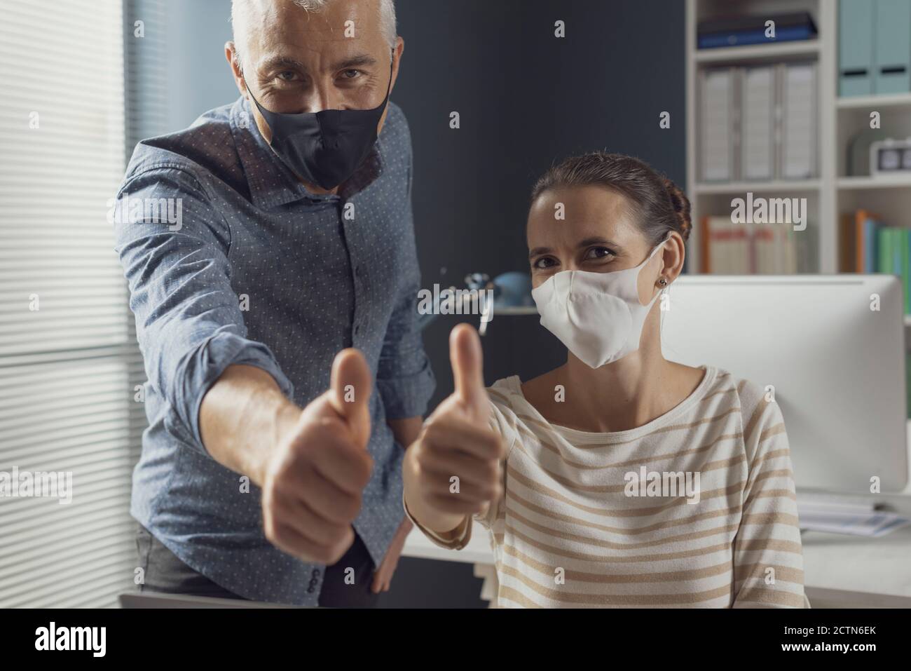 Professional office workers wearing a protective face mask and giving a ...