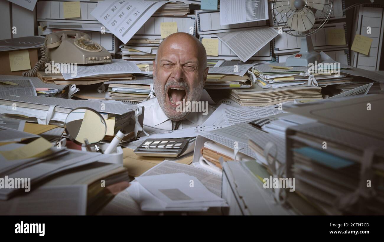 Stressed businessman buried under a lot of paperwork, he is angry and ...