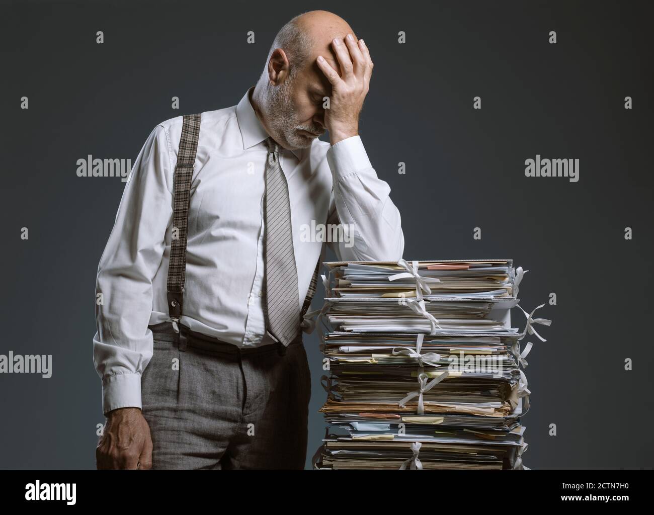 Pensive worried businessman leaning on a pile of paperwork, bureaucracy ...