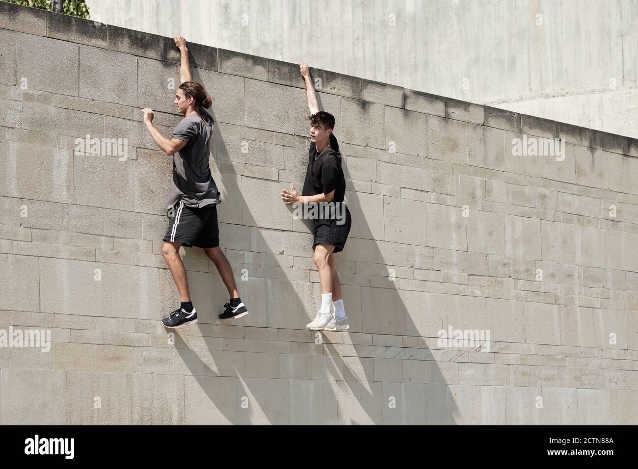 Side view of brave male friends hanging on wall of concrete building ...