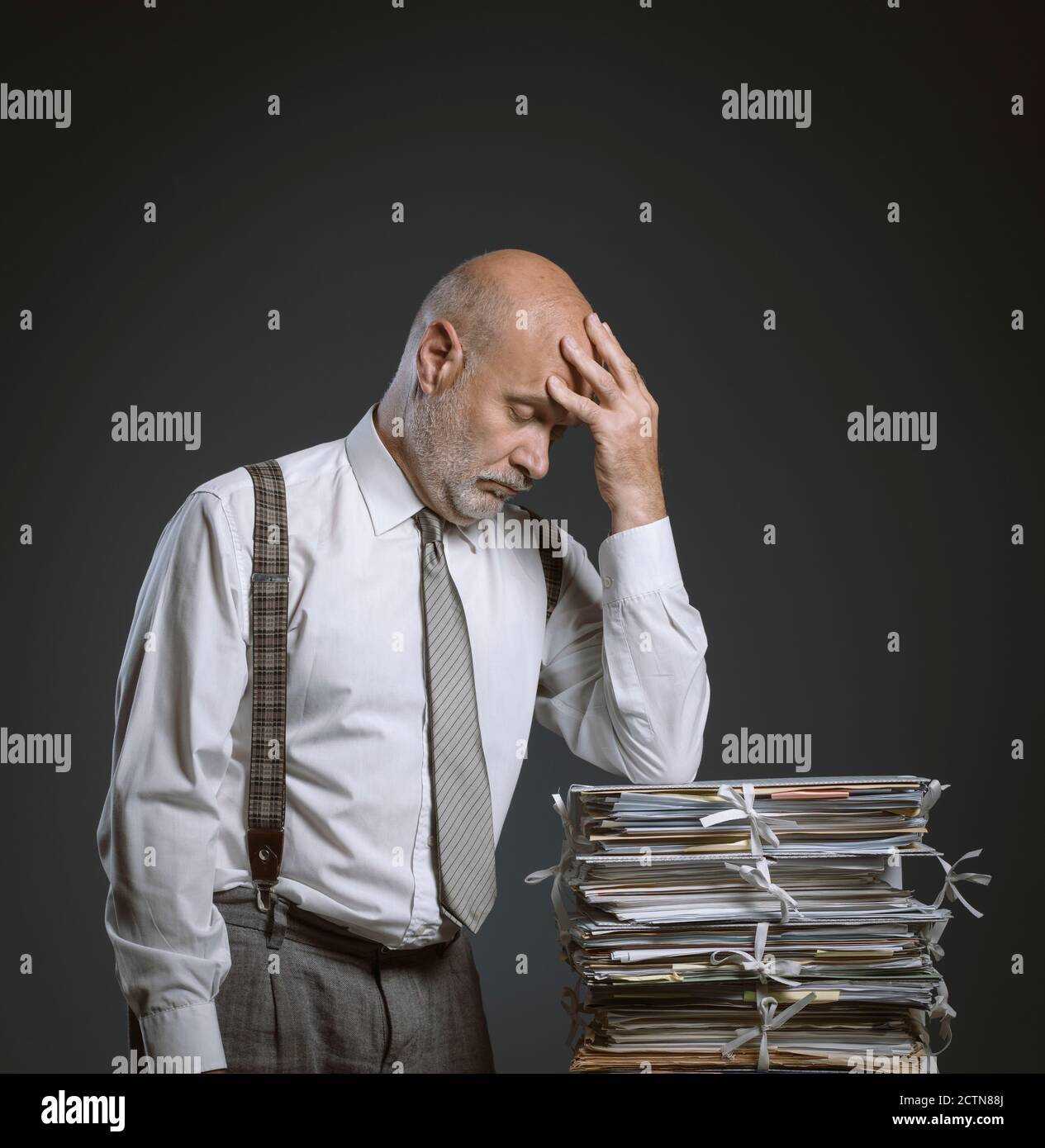 Pensive worried businessman leaning on a pile of paperwork, bureaucracy ...