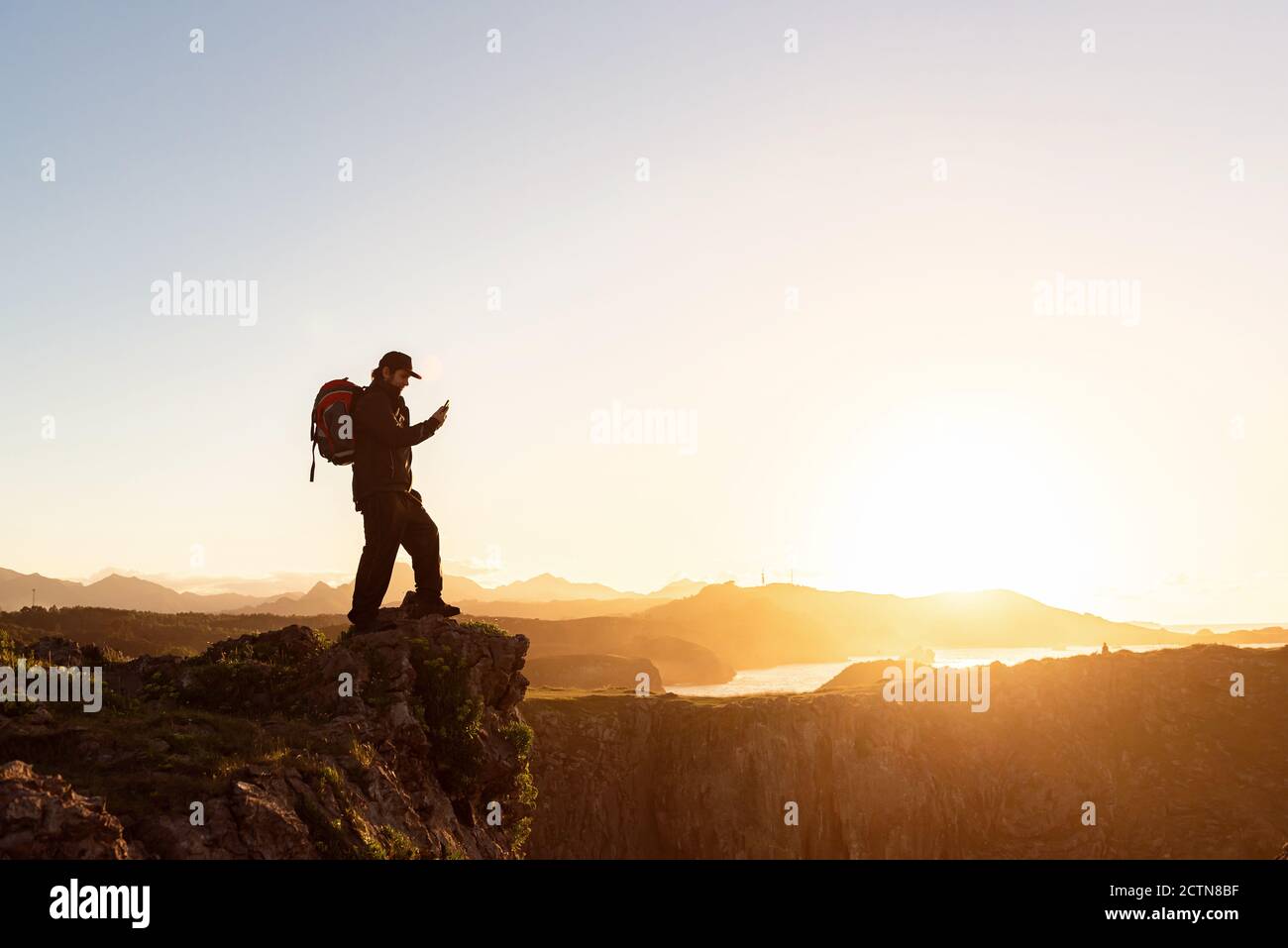 Side view of male explorer with backpack standing on rocky hill and ...