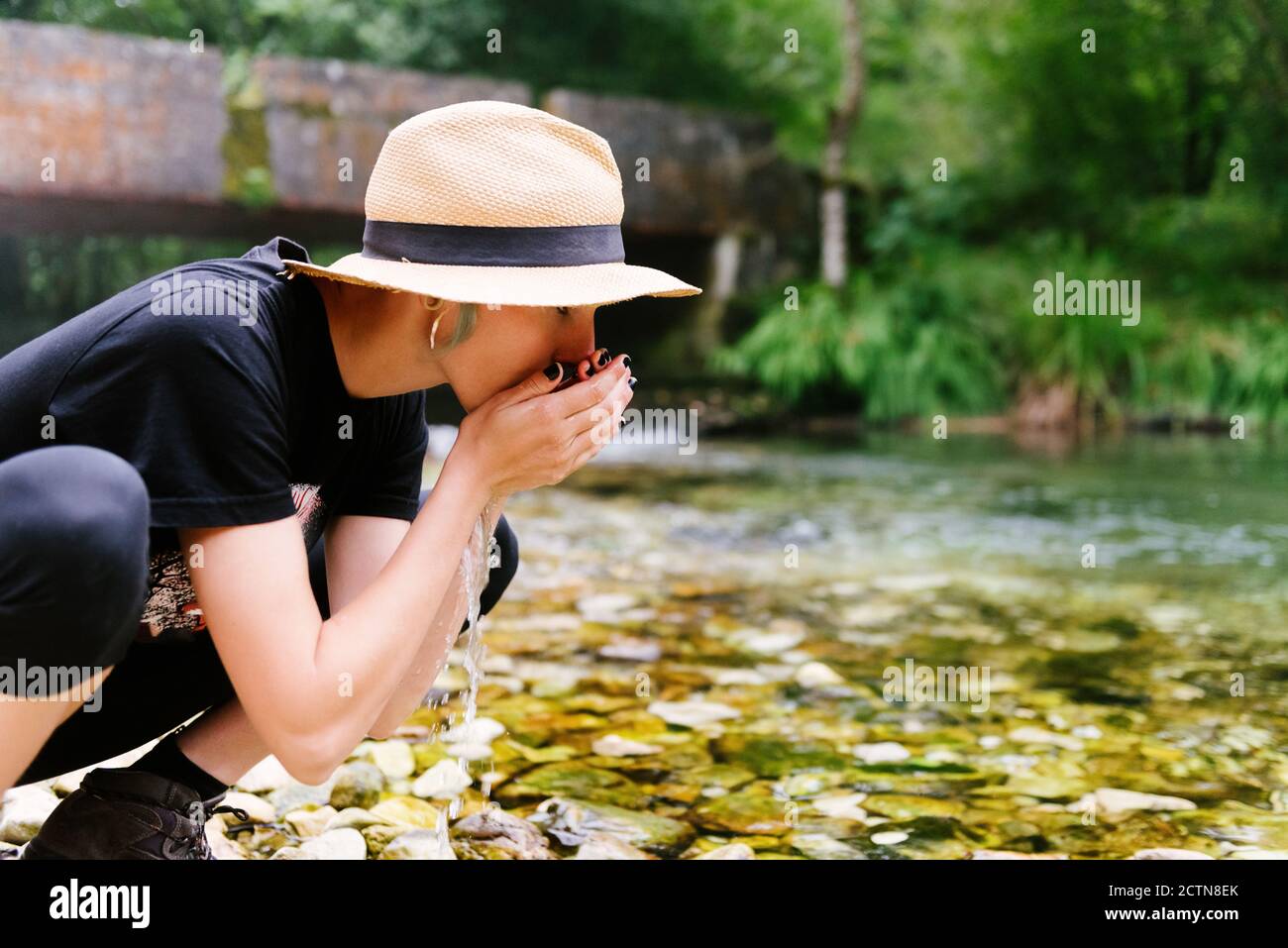 Side view of female tourist drinking clear water from calm river in ...