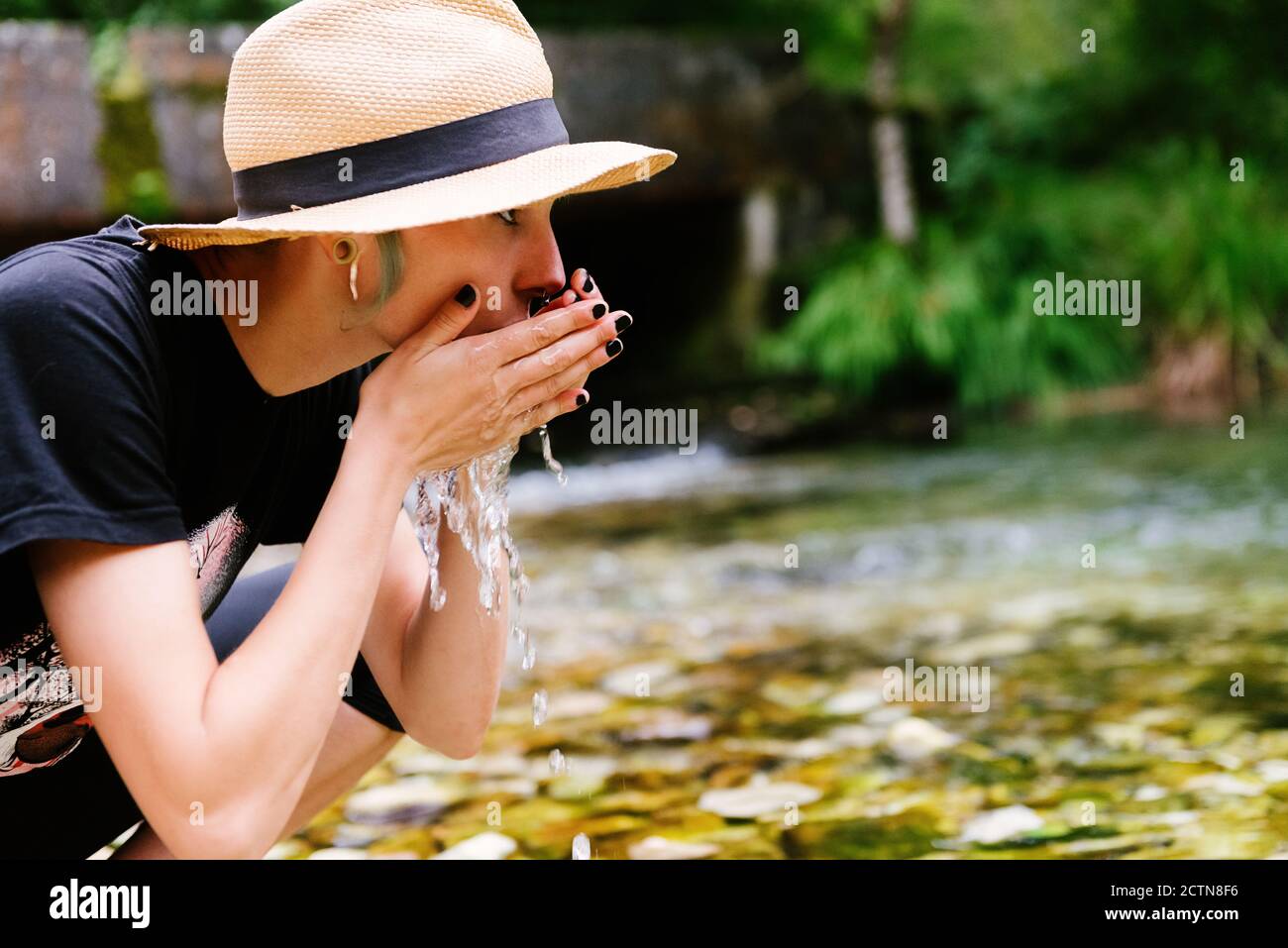 Side view of female tourist drinking clear water from calm river in ...