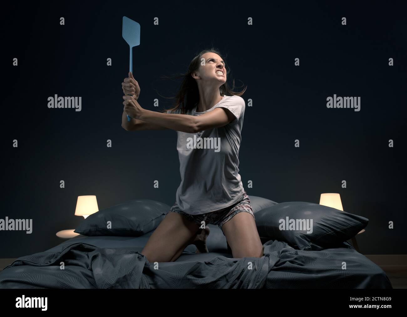 Angry woman killing mosquitoes in her bedroom, she is sitting on the ...