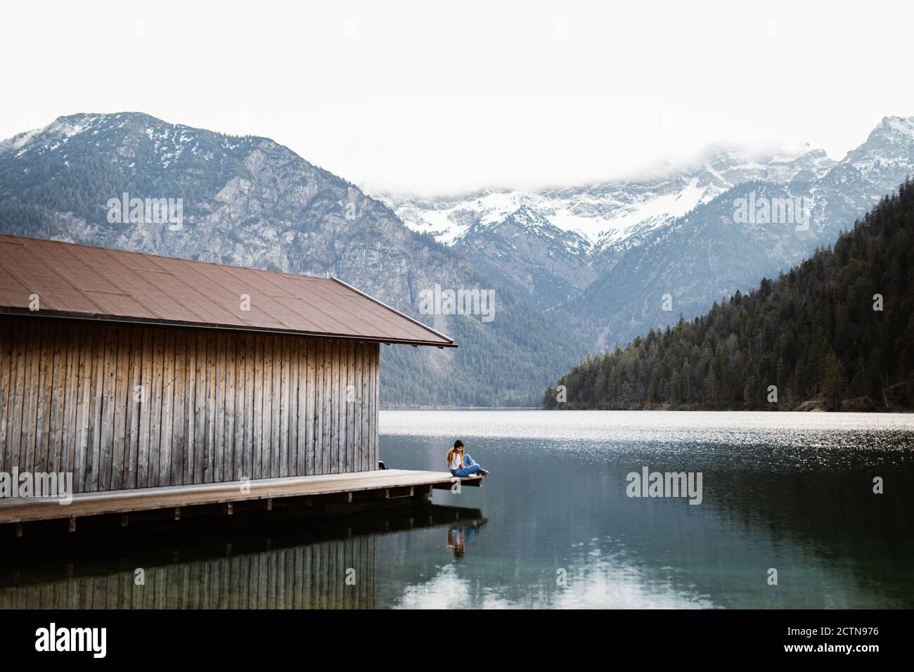 Side view of female sitting on wooden quay and enjoying scenery of calm ...